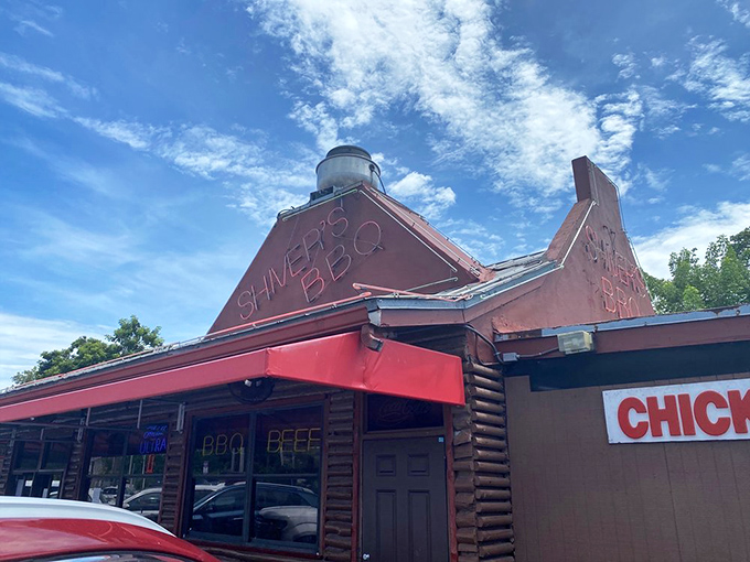 The rustic log cabin exterior of Shiver's BBQ stands as a beacon of smoky promise with its distinctive red trim and wooden fa&ccedil;ade.
