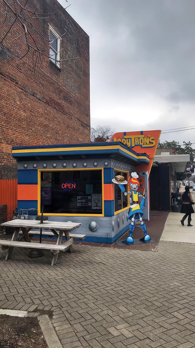 The cosmic facade of Lady Tron's beckons hungry space travelers with its vibrant blue and orange panels. Lady Tron herself stands guard, sandwich in hand.