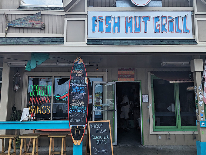 The colorful exterior of Fish Hut Grill beckons hungry beachgoers with its vibrant awning and casual picnic tables—seafood paradise found!