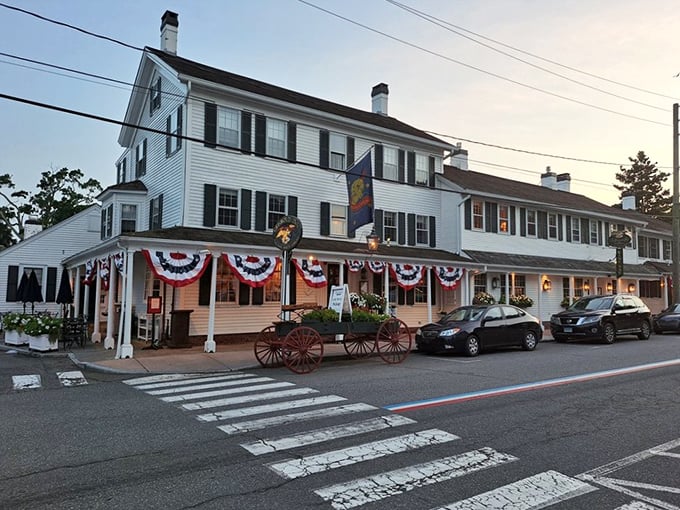 The white clapboard exterior of The Griswold Inn stands proudly in Essex, its patriotic bunting and antique wagon announcing: history happened here, and it was delicious.