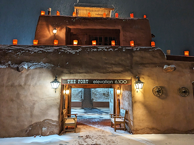 The Fort's adobe entrance glows with warmth against the night sky, luminous farolitos beckoning hungry travelers to step back in time at 6,100 feet elevation.
