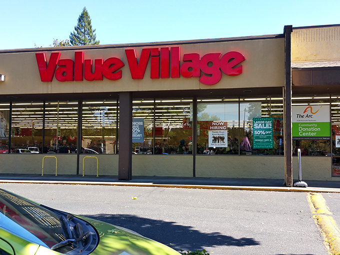 The iconic red Value Village sign beckons like a lighthouse for bargain hunters navigating the sea of retail sameness.
