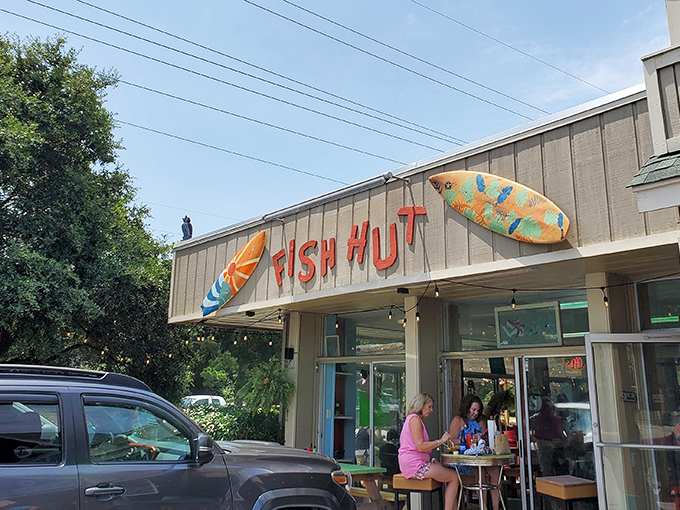 The colorful exterior of Fish Hut Grill beckons hungry beachgoers with its vibrant awning and casual picnic tables&mdash;seafood paradise found! 