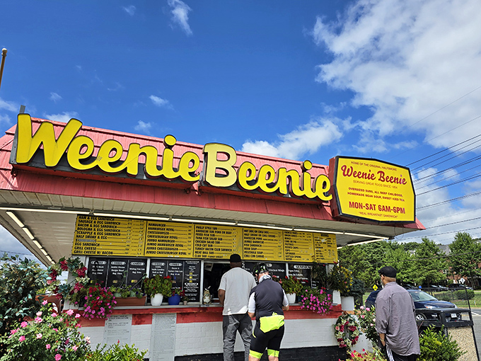 The iconic pink-and-yellow Weenie Beenie stands proudly against a blue Virginia sky, like a time capsule of American roadside charm waiting to be discovered.