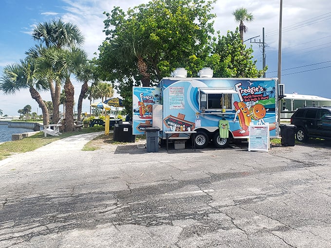 Paradise found: A cheerful blue food truck nestled among palm trees, where waterfront views come standard with every hot dog order.