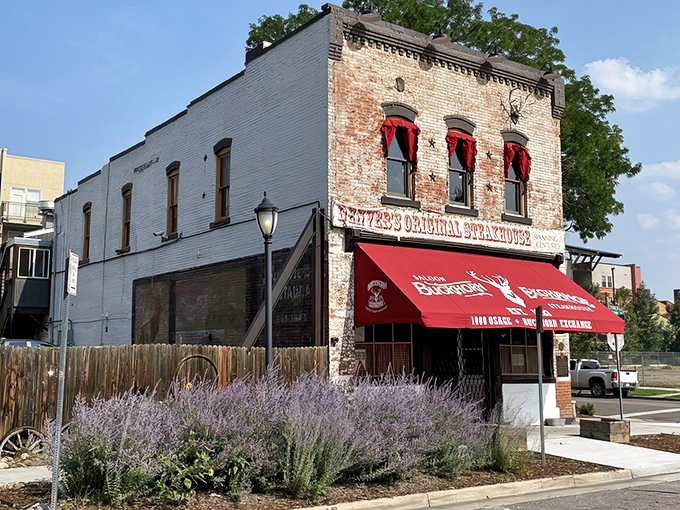 The brick facade of Buckhorn Exchange glows under night lights, its iconic red awning beckoning hungry travelers like a carnivorous lighthouse in urban Denver.