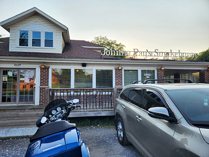 The welcoming glow of Johnny Ray's Smokehouse beckons hungry travelers with its homey brick exterior and cozy wooden deck&mdash;barbecue paradise found. 