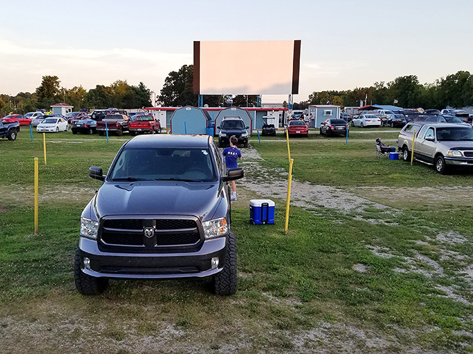 Cars aligned in perfect movie-watching formation as dusk approaches. Some visitors come early to claim prime viewing spots with blankets and lawn chairs. 