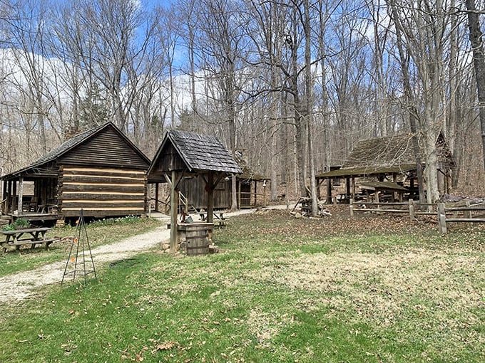 Historic log cabins nestled among bare trees tell stories of pioneer life, creating an open-air time machine just steps from the trail.