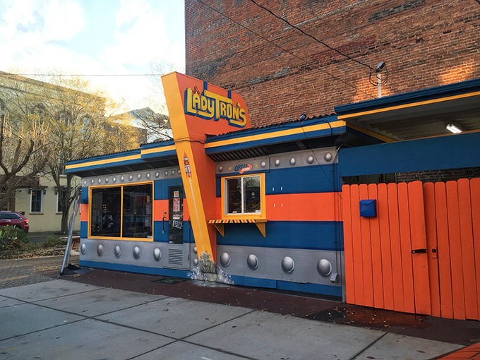 The cosmic facade of Lady Tron's beckons hungry space travelers with its vibrant blue and orange panels. Lady Tron herself stands guard, sandwich in hand.