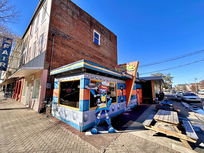 The cosmic facade of Lady Tron's beckons hungry space travelers with its vibrant blue and orange panels. Lady Tron herself stands guard, sandwich in hand.