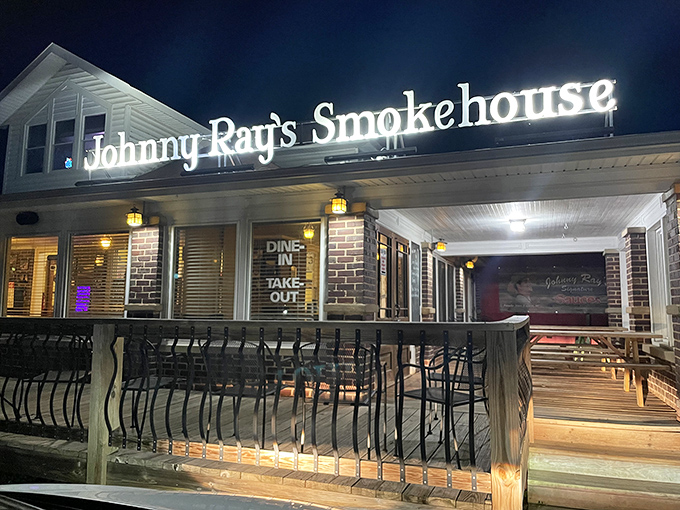 The welcoming glow of Johnny Ray's Smokehouse beckons hungry travelers with its homey brick exterior and cozy wooden deck—barbecue paradise found.