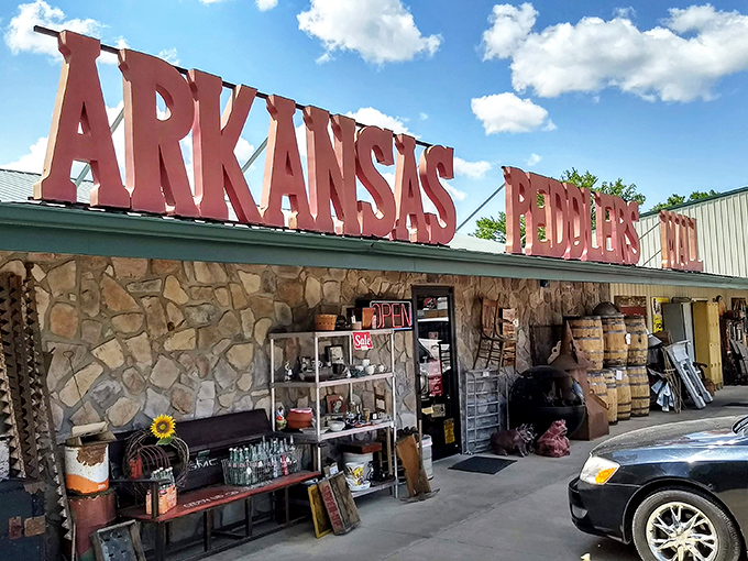 The bright red letters of Arkansas Peddlers stand like a welcoming carnival barker against the sky, with that charming green dinosaur keeping watch over vintage treasures.