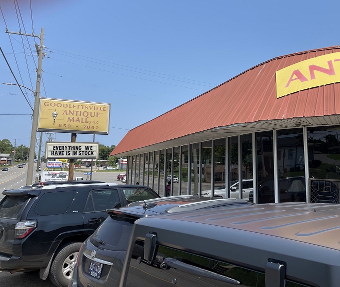 Peek down a corridor of curiosities where treasure hunters navigate a sea of vintage wonders under the watchful eye of a blue bicycle suspended in mid-flight.