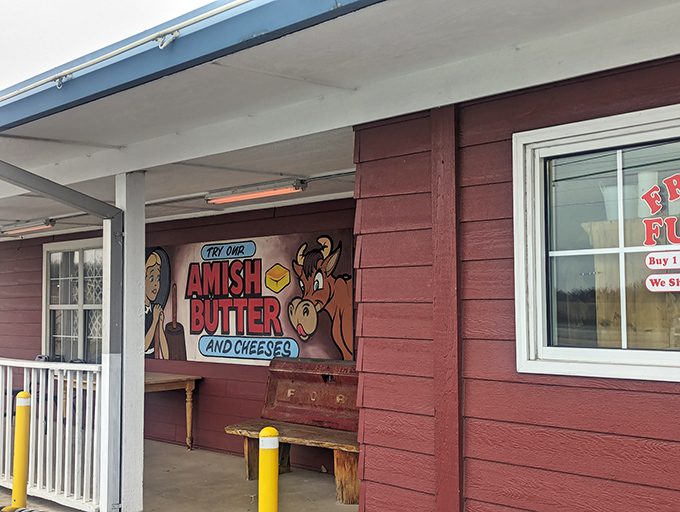 The unassuming burgundy exterior with its "Try our Amish Butter and Cheeses" sign promises treasures within that the simple facade modestly conceals.