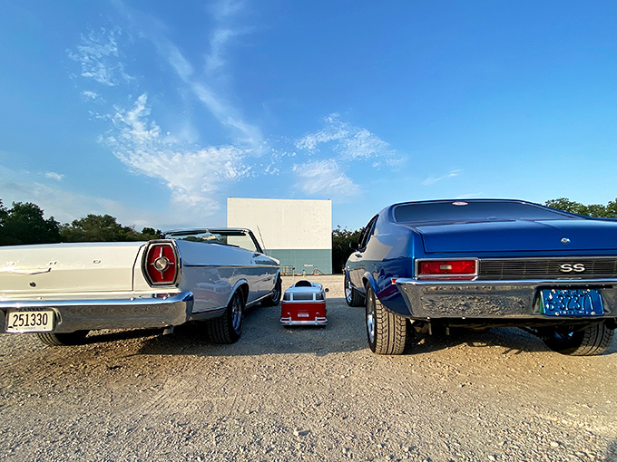 Classic American cars flank a tiny pedal car, three generations of automotive history facing the silver screen&mdash;nostalgia in its purest form.