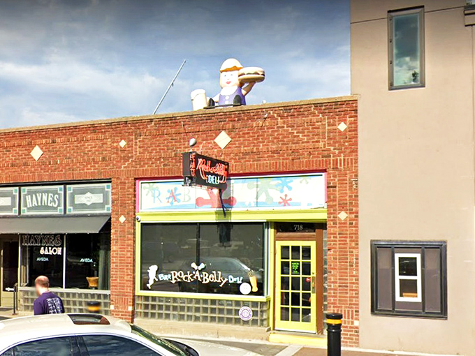 The bright yellow door acts like a portal to flavor town, with that whimsical sandwich figure on the roof standing guard over culinary treasures below.