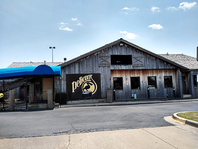 The weathered wooden exterior of Pelican's Restaurant stands like a coastal mirage in Midwest City, complete with signature blue awning and rustic charm.