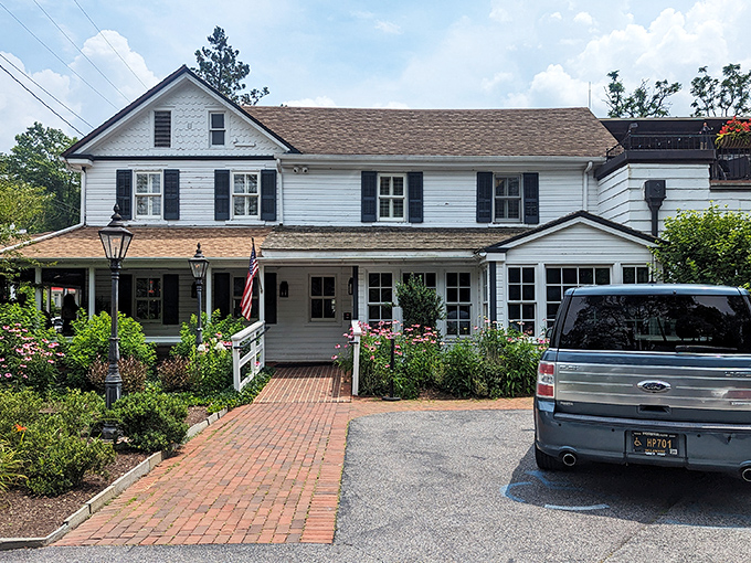 The historic white clapboard exterior of Buckley's Tavern welcomes visitors with lush greenery and brick pathways, a Delaware landmark since the 1700s.