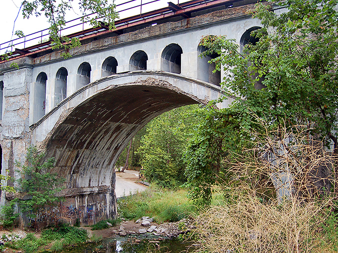The weathered arches of Avon's Haunted Bridge stand sentinel against an autumn sky, where concrete and legend have intertwined for generations.