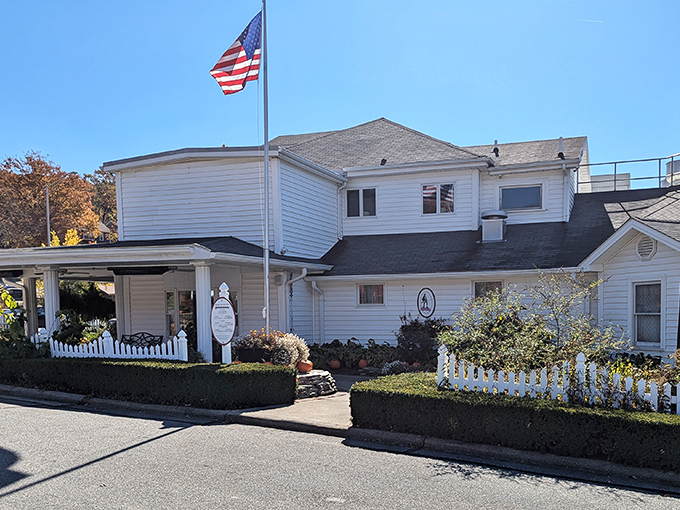 The white clapboard building with its picket fence and American flag stands as a testament to timeless Appalachian hospitality in downtown Boone.