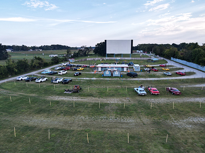 Cars aligned in perfect movie-watching formation as dusk approaches. Some visitors come early to claim prime viewing spots with blankets and lawn chairs. 
