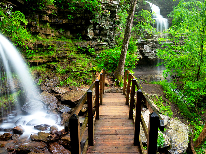 Nature's perfect postcard moment: a rustic wooden bridge leads you between cascading waterfalls, promising adventure with every step into this emerald paradise.