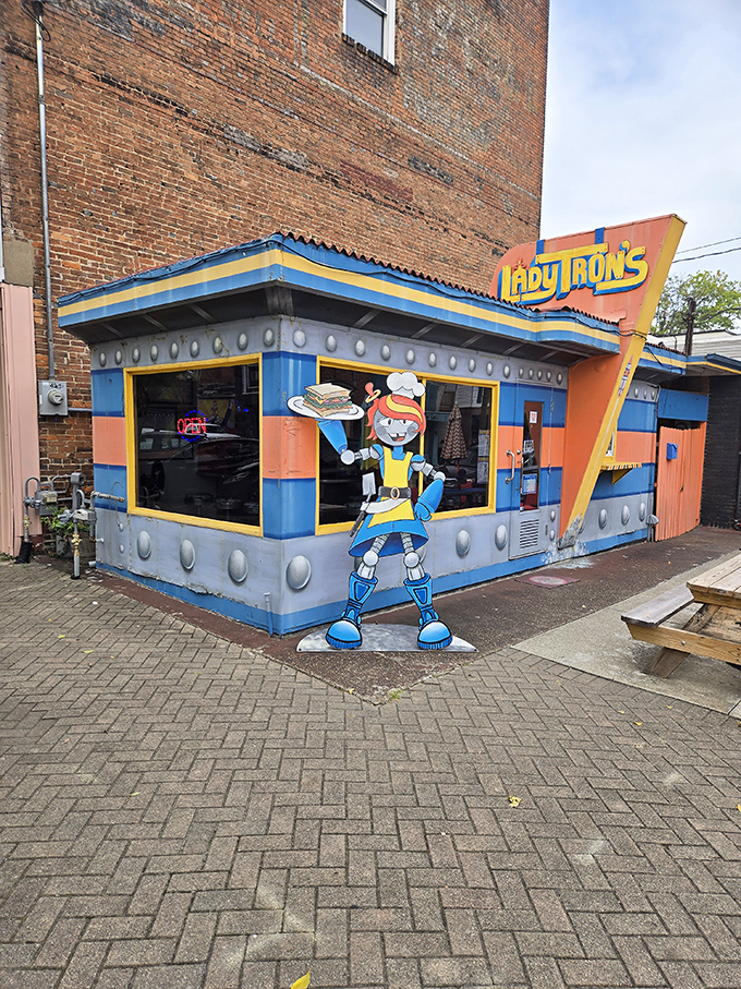 The cosmic facade of Lady Tron's beckons hungry space travelers with its vibrant blue and orange panels. Lady Tron herself stands guard, sandwich in hand.