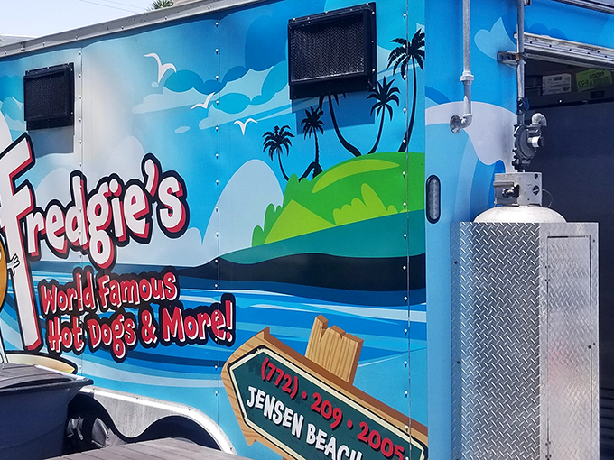 Paradise found: A cheerful blue food truck nestled among palm trees, where waterfront views come standard with every hot dog order.
