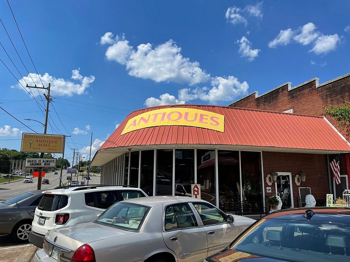 Peek down a corridor of curiosities where treasure hunters navigate a sea of vintage wonders under the watchful eye of a blue bicycle suspended in mid-flight. 