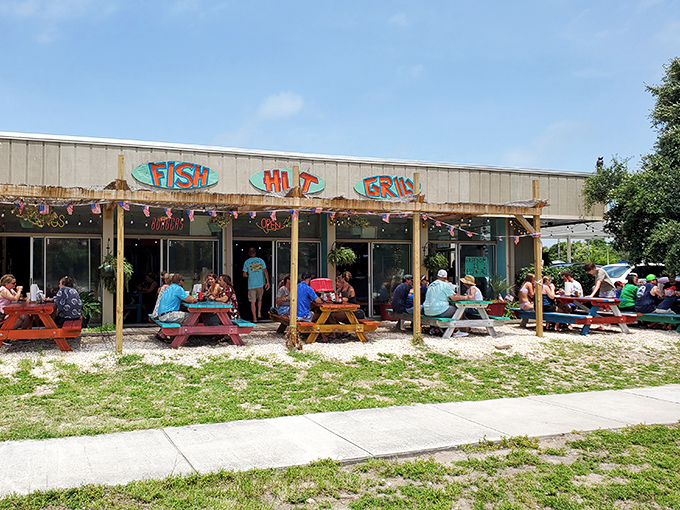 The colorful exterior of Fish Hut Grill beckons hungry beachgoers with its vibrant awning and casual picnic tables—seafood paradise found!