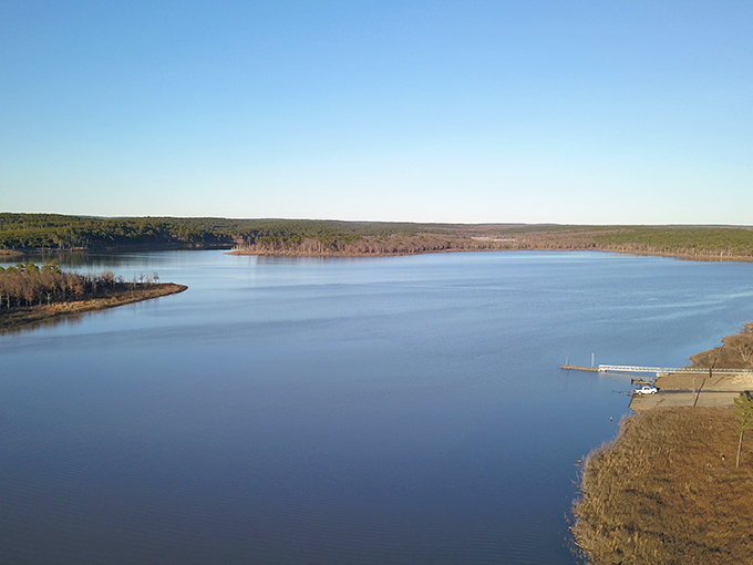 Mirror-like waters reflect the forested shoreline at McGee Creek Reservoir, where silence is only broken by the occasional splash of a jumping bass.