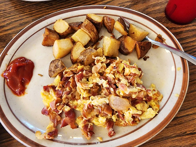 Morning magic on a plate: scrambled eggs dancing with bacon bits alongside home fries that somehow manage to be both crispy and tender.