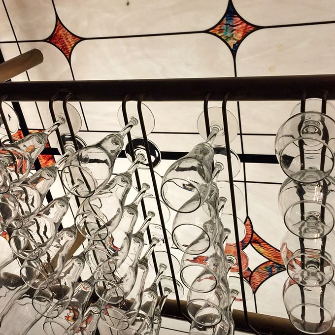 Elegant rows of gleaming glassware hang beneath a stained-glass ceiling, adding vintage charm to the historic atmosphere of this beloved Virginia restaurant.