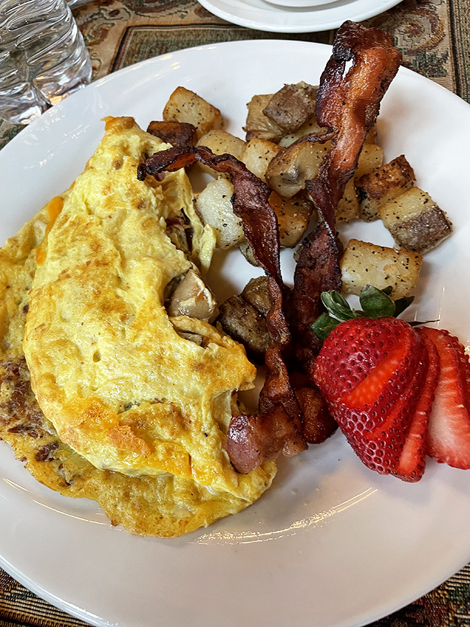 Morning masterpiece: A perfectly crafted omelet alongside crispy bacon, seasoned potatoes, and fresh strawberries &ndash; breakfast that makes you forget to check your phone.