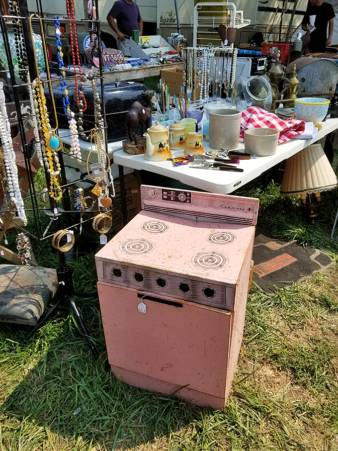A pink vintage stove sits among costume jewelry and lampshades&mdash;someone's childhood kitchen appliance now waits for its second act as retro decor.