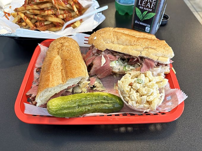 This sandwich means business - layers of rosy pastrami, crisp pickle spear, and potato salad on the side. Lunch dreams come true on a red tray.