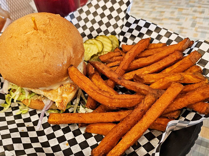 Sweet potato fries standing at attention beside a burger that's clearly living its best life. The pickle chips are like little tangy sentinels guarding flavor paradise.