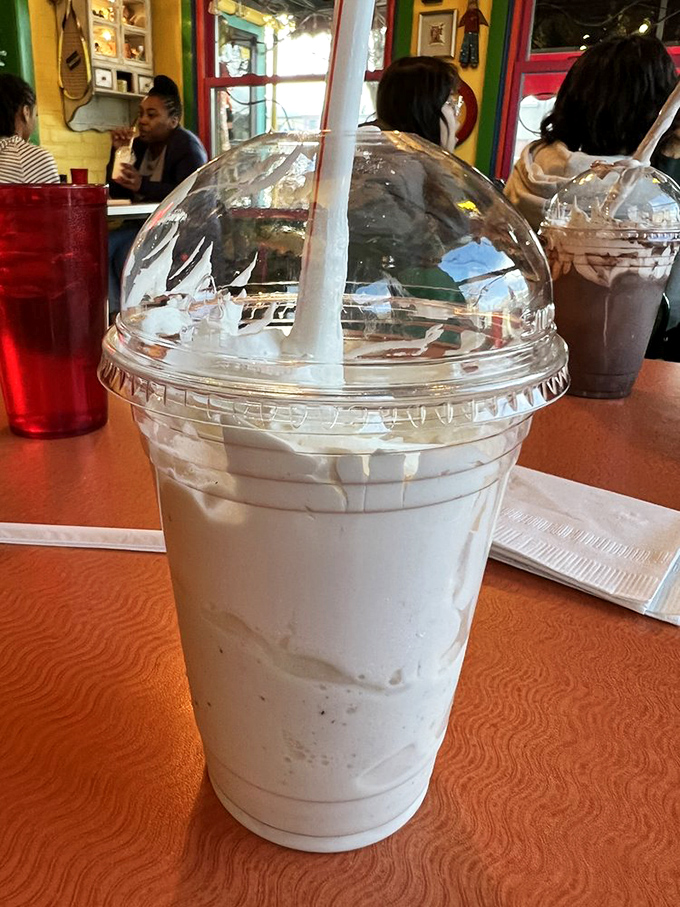 The vanilla milkshake arrives in a plastic dome like a dairy snow globe. Thick enough to require both straw and spoon diplomacy.
