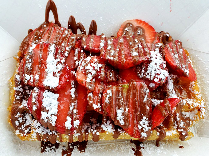 Fresh strawberries, powdered sugar, and chocolate drizzle transform a simple waffle into something that belongs in a museum of breakfast art.