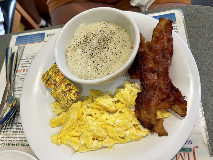 A trifecta of breakfast perfection: fluffy scrambled eggs, crispy bacon, and creamy grits that would make any Southerner nod in approval.