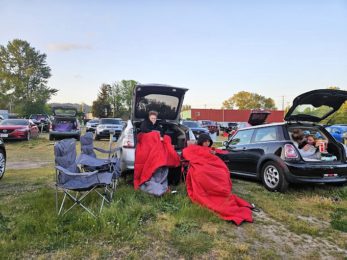 Blankets, lawn chairs, and open hatchbacks transform parking spots into personal living rooms under the canvas of Oregon's evening sky.