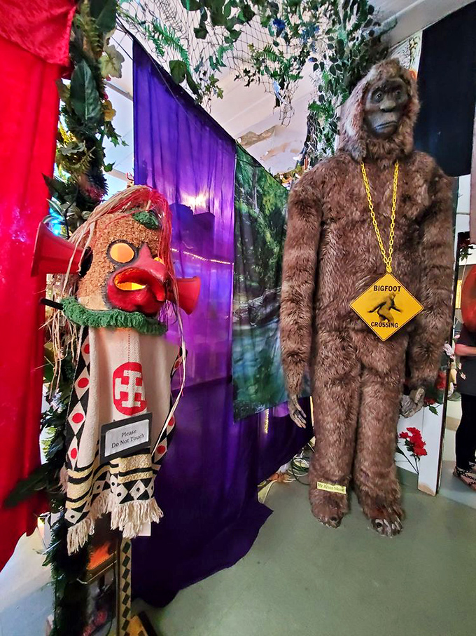 Bigfoot, sporting his "Crossing" sign necklace, stands ready for selfies beside what appears to be a tribal artifact.