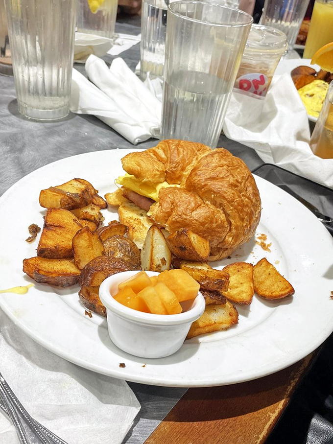 A golden croissant sandwich surrounded by breakfast potatoes &ndash; proof that not all heroes wear capes, some wear flaky layers.