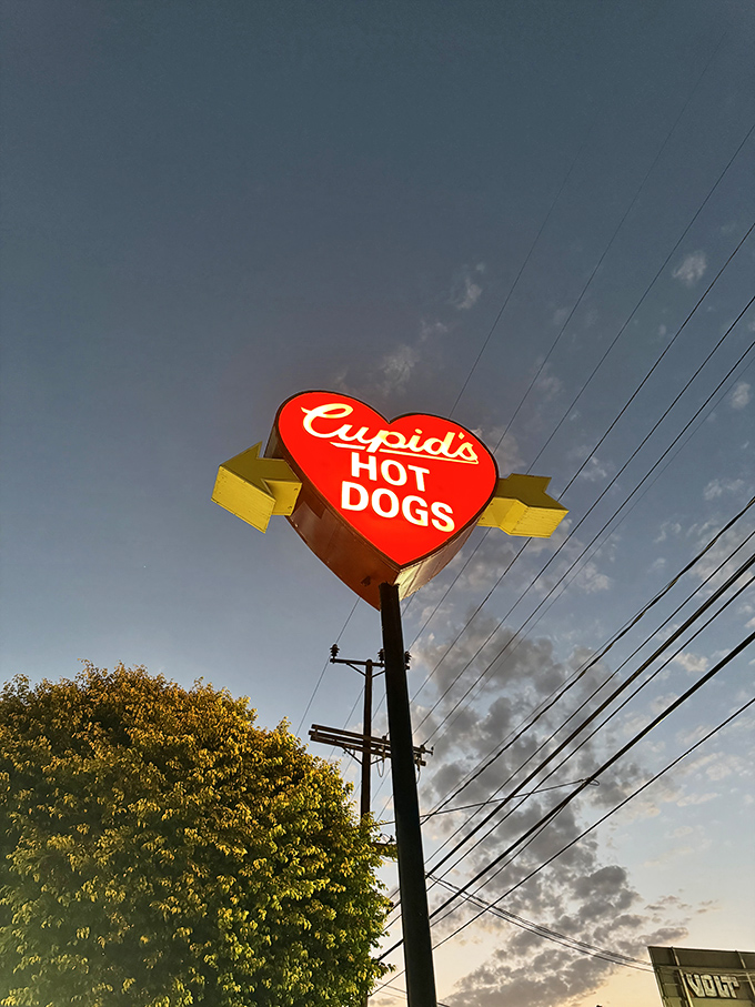 As dusk settles, the heart-shaped sign glows like a beacon of hope for the hungry. Some lighthouses guide ships; this one guides appetites.