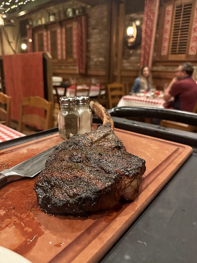 This magnificent tomahawk ribeye arrives on a wooden board like a carnivore's trophy, resting dramatically against the rustic backdrop of checkered tablecloths.