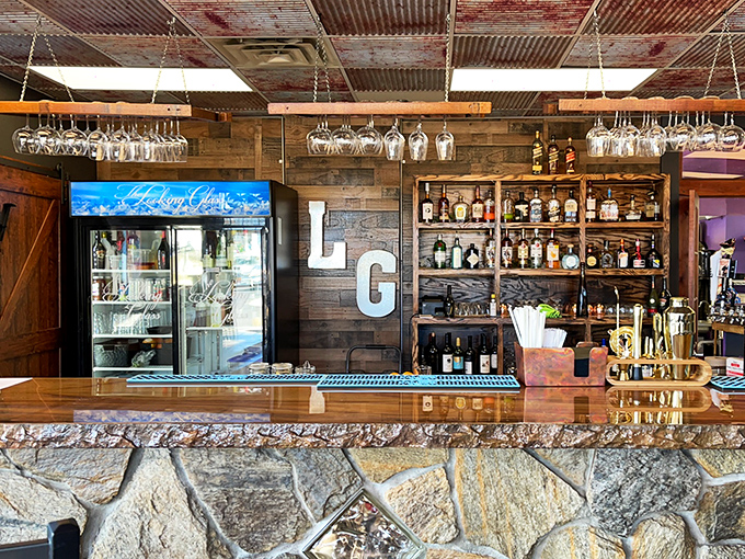 The bar area blends rustic and refined with corrugated metal ceiling, wine glasses hanging like crystal stalactites, and spirits lined up like characters awaiting their cue.
