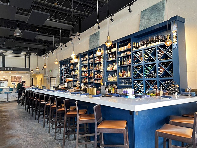 A bar that says "pull up a seat and stay awhile." The blue shelving showcases bottles like treasures from a particularly delicious shipwreck.