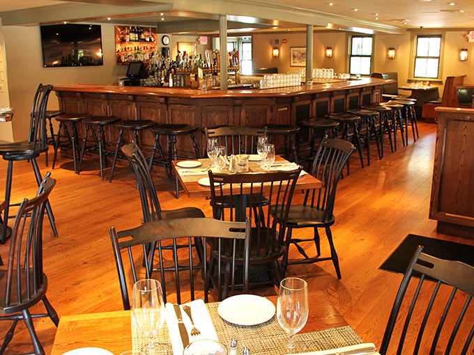The bar area combines rustic wood, classic black chairs, and enough spirits to make even the shyest guest feel like a regular after one perfectly mixed Manhattan.