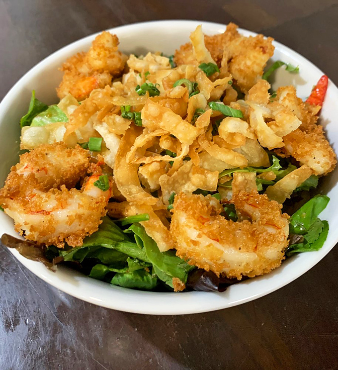 Calamari that defies the rubbery reputation of lesser versions, perched atop greens like crispy golden halos from the sea.